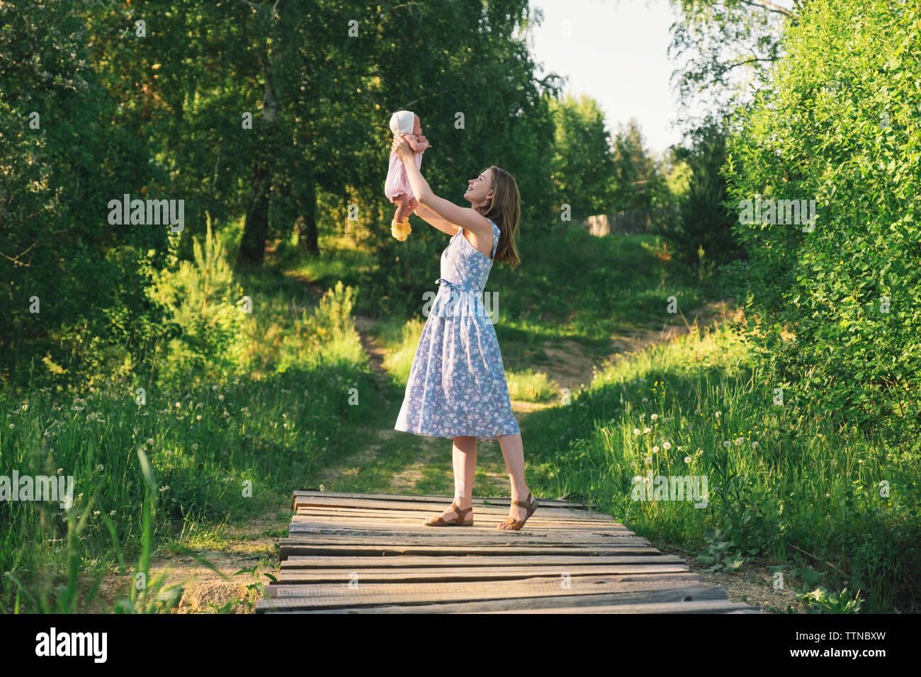 Side view of mother picking up cute newborn daughter while standing on ...