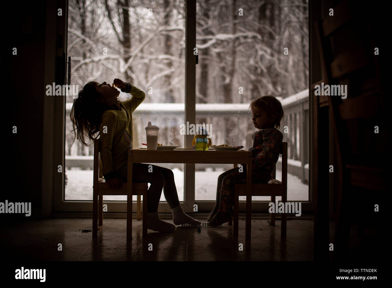 Sisters eating in front of window with snowy view Stock Photo - Alamy