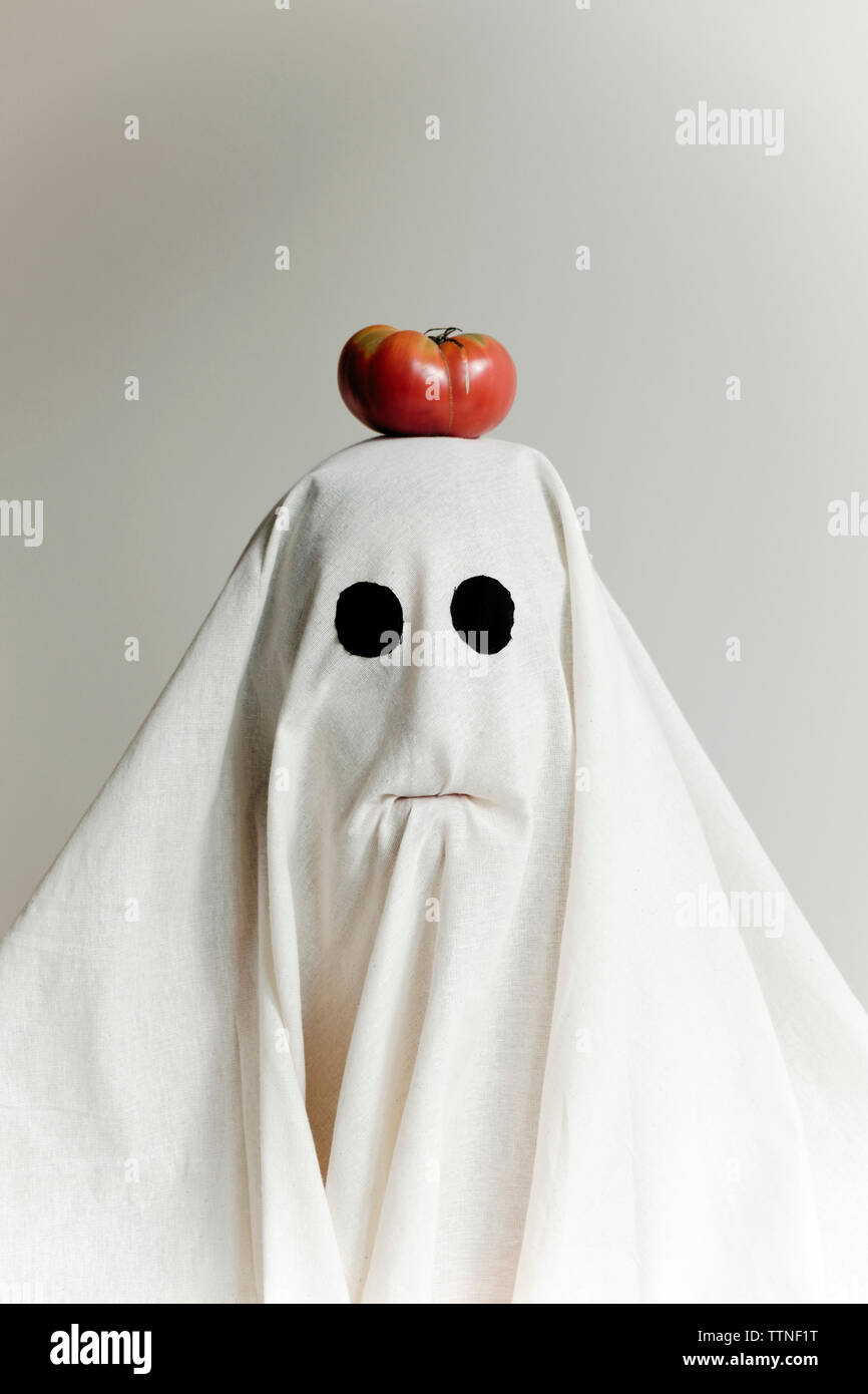 Man in ghost costume carrying squash on head while standing against ...