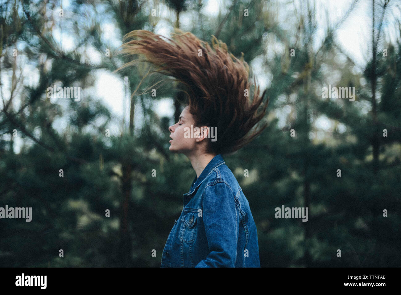 Side view of woman tossing hair while standing in forest Stock Photo ...