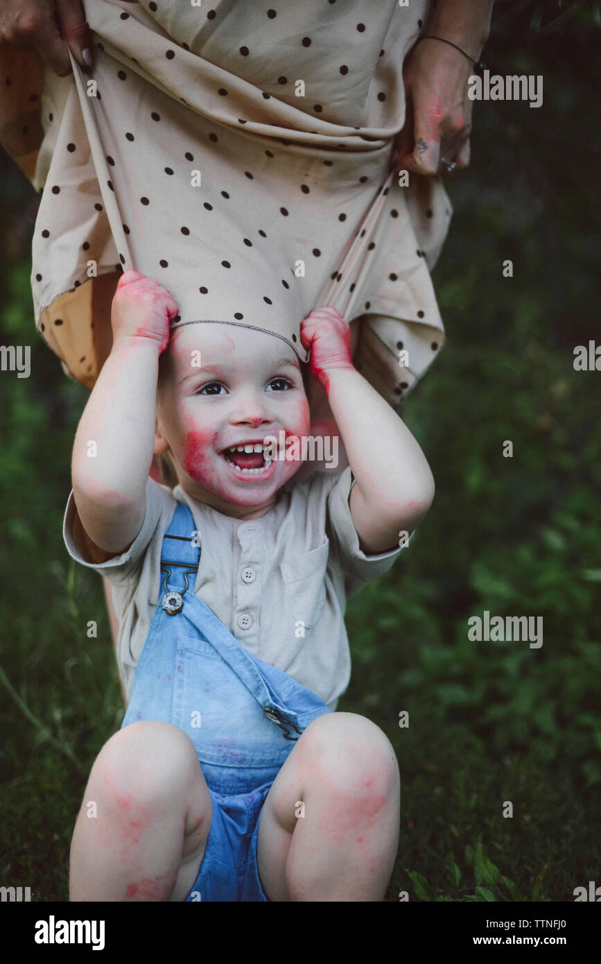 Playful son pulling mother's clothes while crouching in yard Stock ...