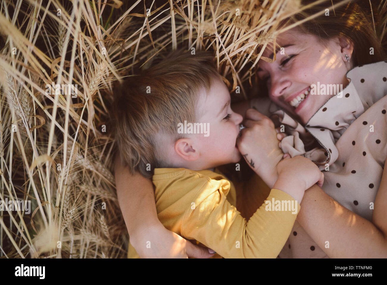 High angle view of playful son biting mother's fingers while lying on ...