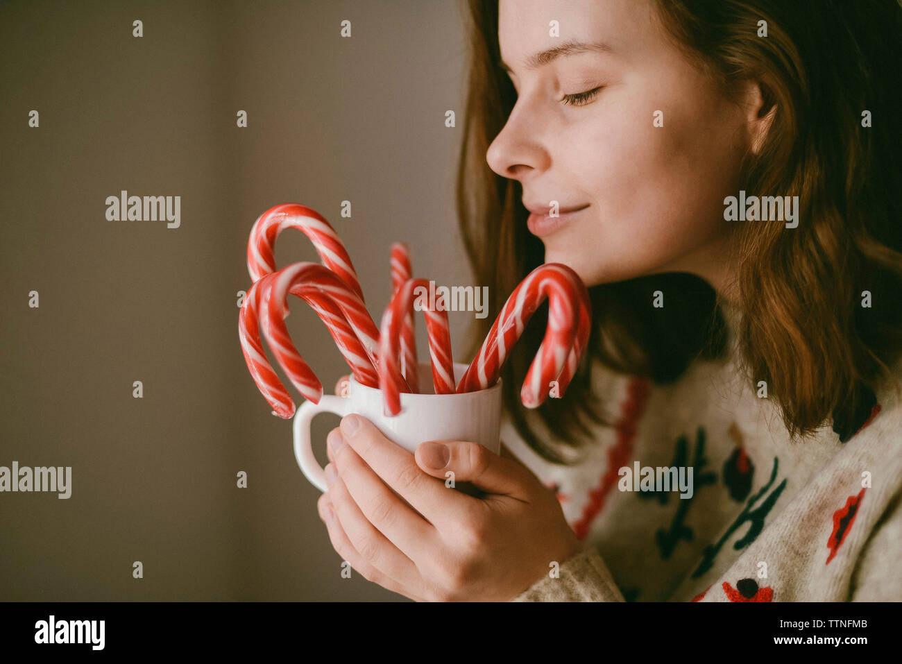 Side view of young woman holding candy canes in cup at home Stock Photo ...