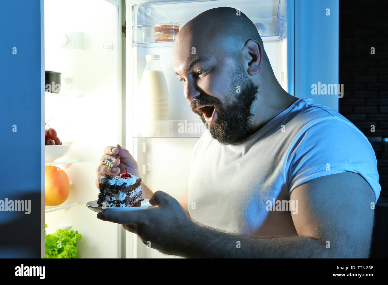 Man eating at night next to refrigerator Stock Photo - Alamy