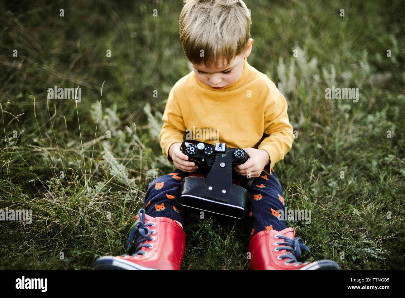 Boy with camera while sitting on grassy field Stock Photo - Alamy