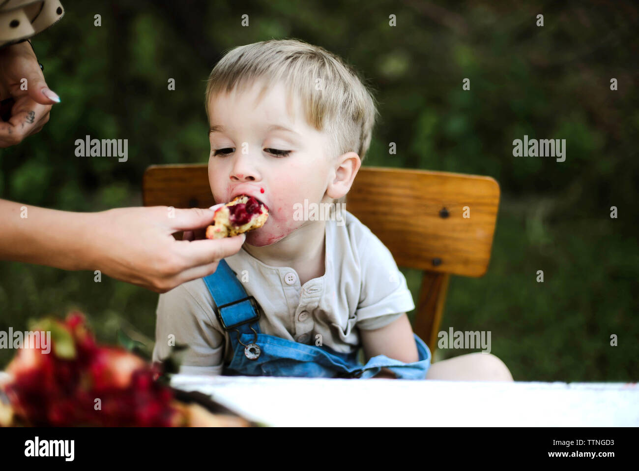 Cropped hand of mother feeding sweet pie to son sitting on chai Stock ...