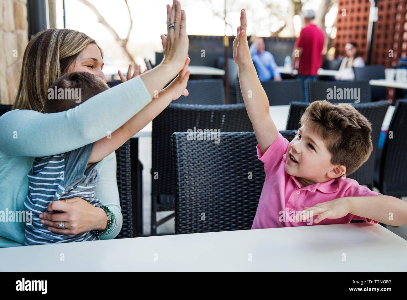 Mother and sons giving high-five at restaurant table Stock Photo - Alamy