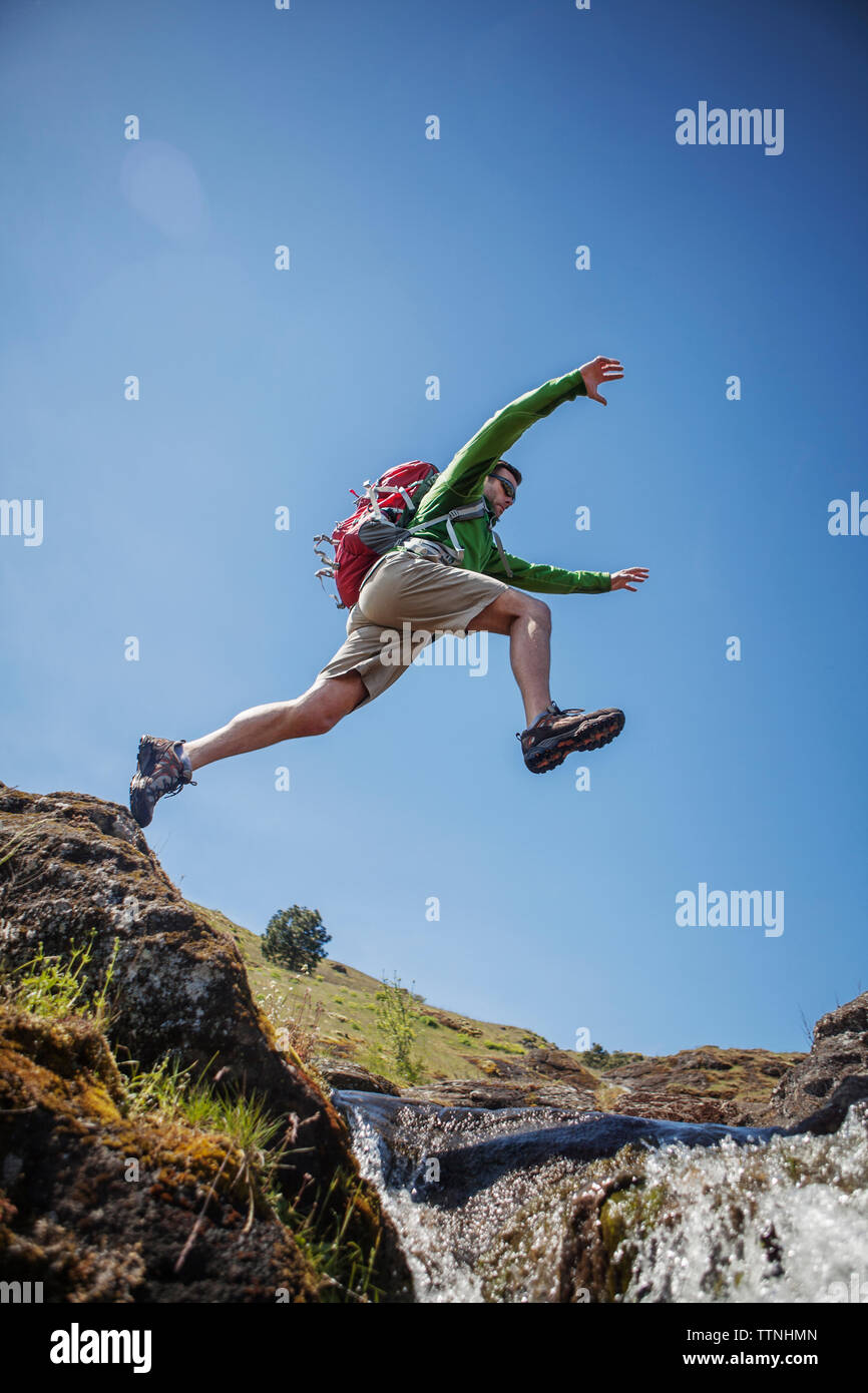 Low angle view of male hiker jumping over stream Stock Photo - Alamy