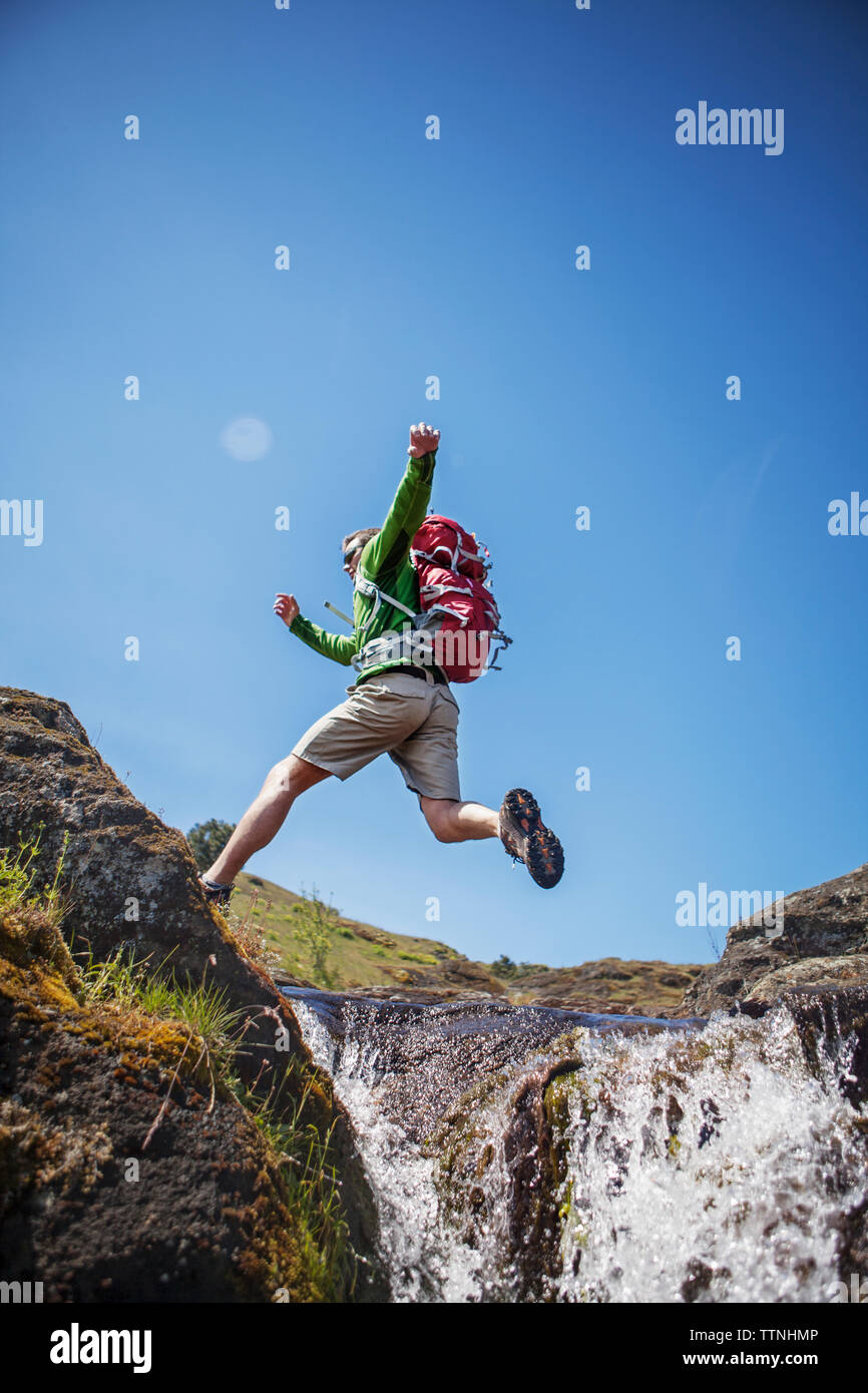 Carefree hiker jumping over stream against clear sky Stock Photo - Alamy