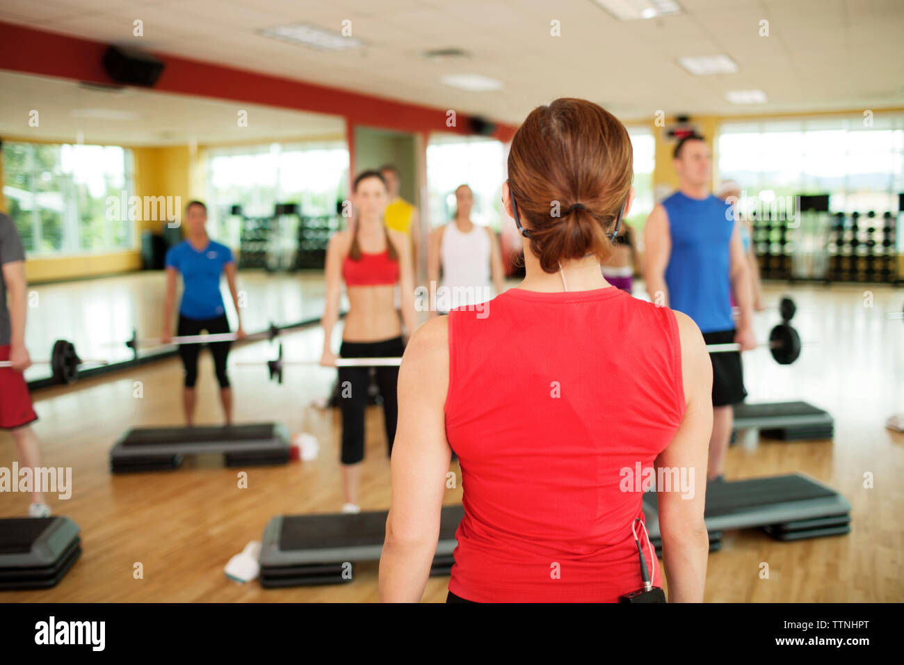 Rear view instructor with clients lifting barbells by steps in health ...