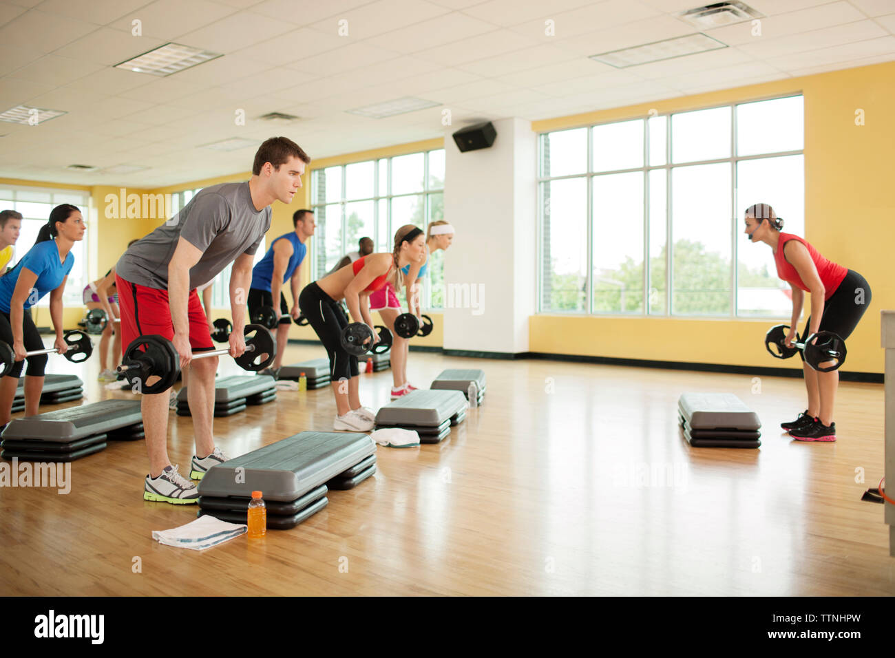 Instructor and clients lifting barbells by steps in gym Stock Photo - Alamy