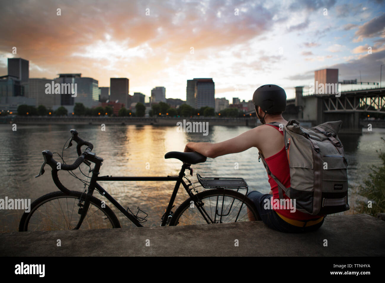Athlete carrying backpack while sitting on retaining wall by lake Stock ...