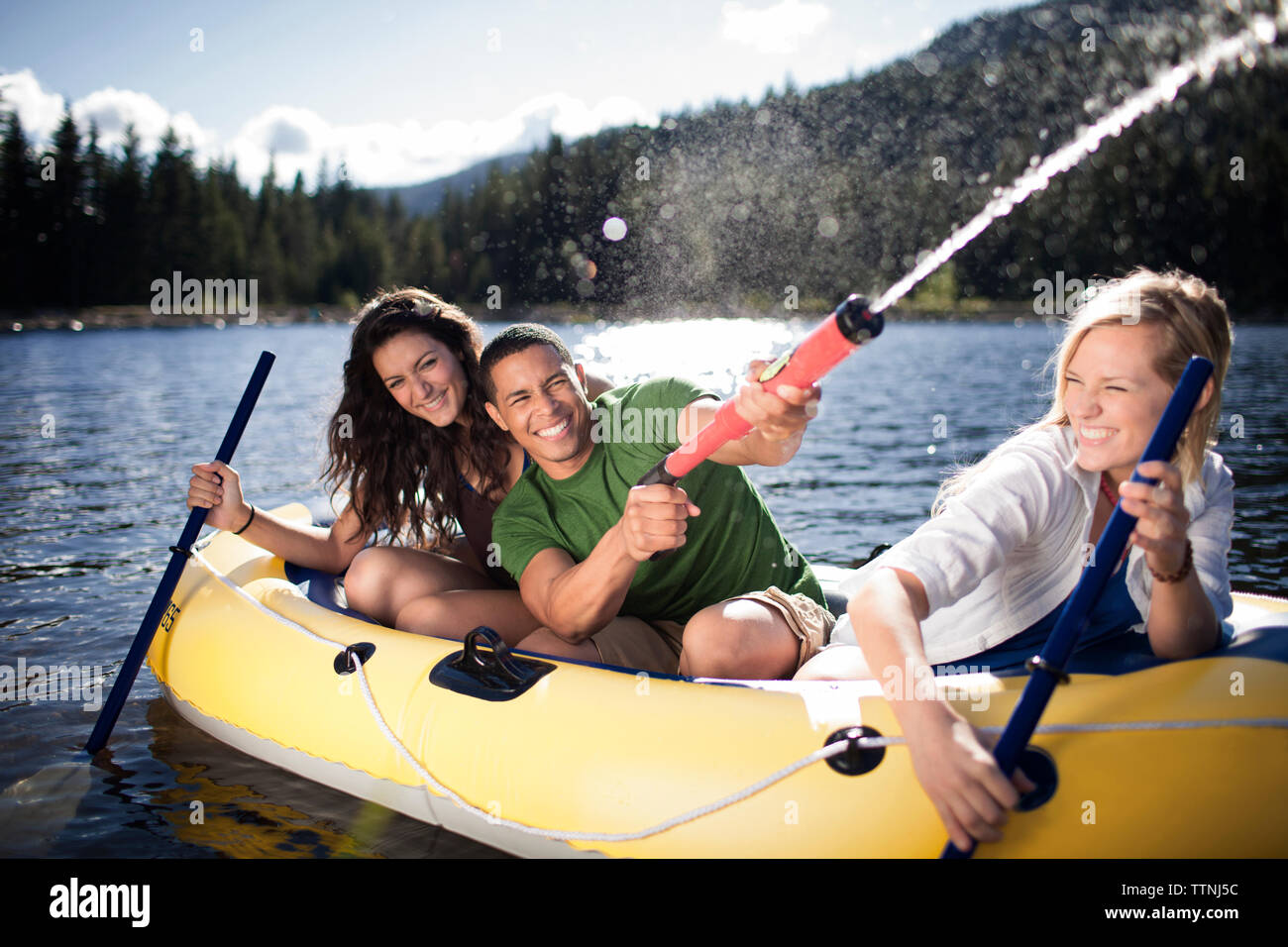 Man spraying water with squirt gun while sitting by female friends in ...