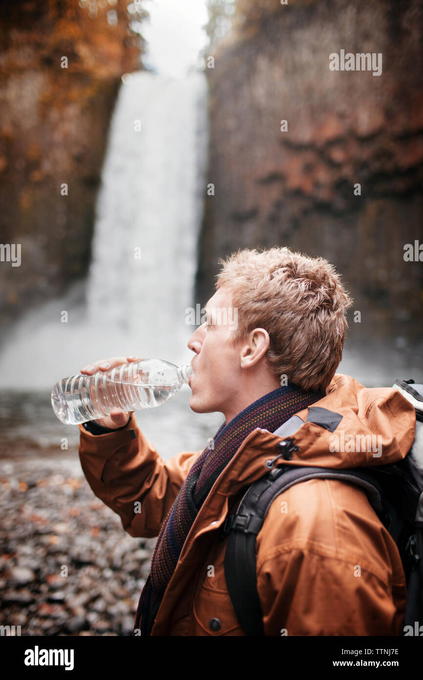 Side view of male hiker drinking water from bottle while standing ...