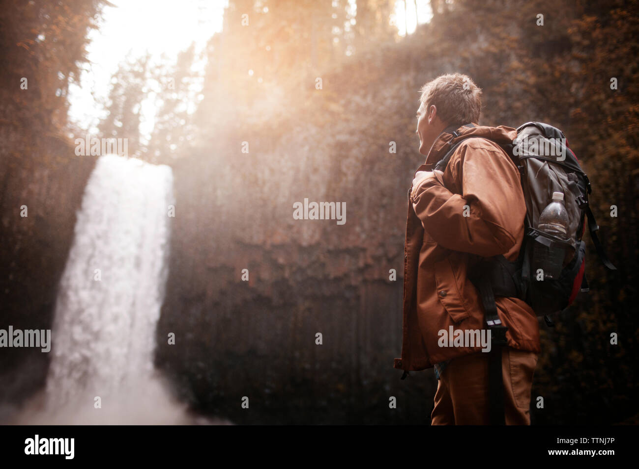 Side view of hiker carrying backpack while looking at waterfall Stock ...