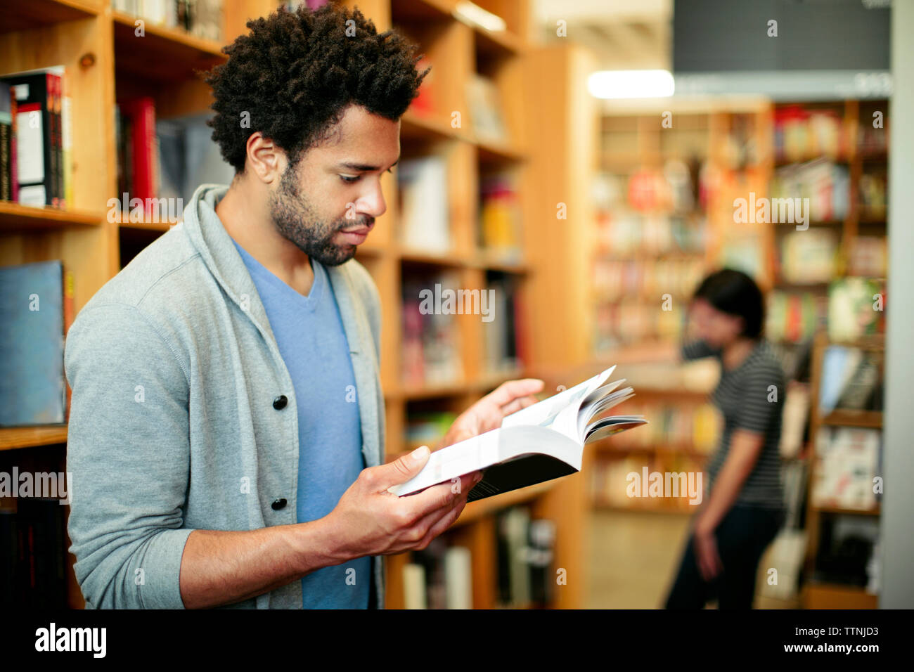 Man reading book in library with woman standing in background Stock ...