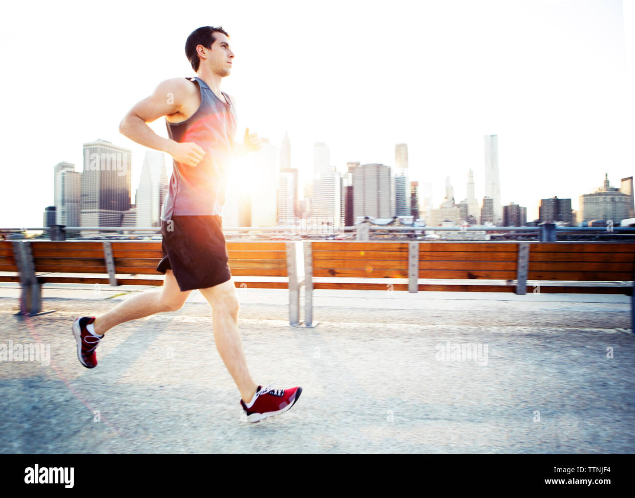 Side view of man running by bench against cityscape Stock Photo - Alamy