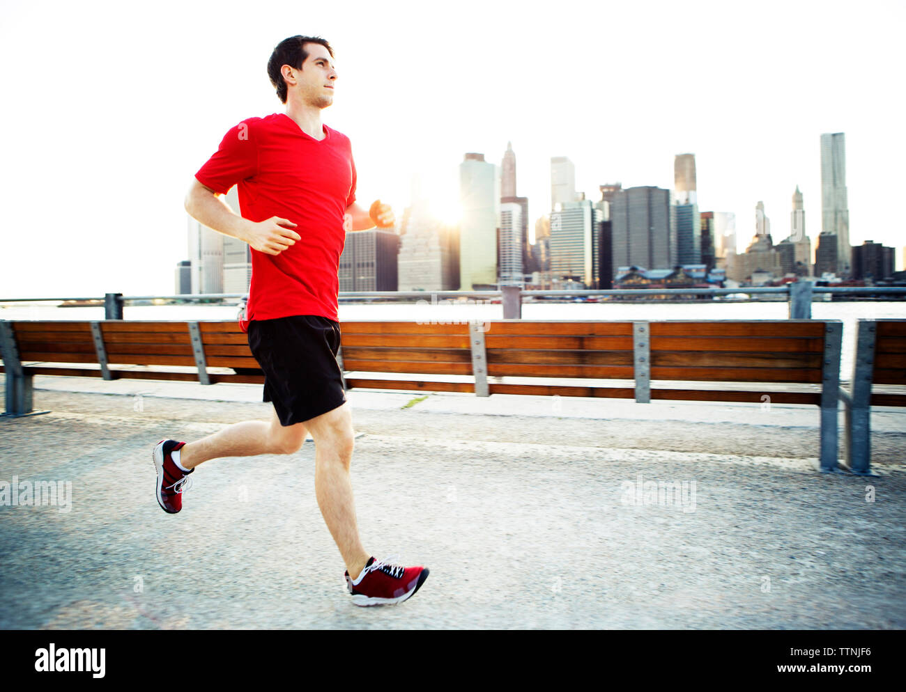 Man running by bench at riverbank against cityscape Stock Photo - Alamy