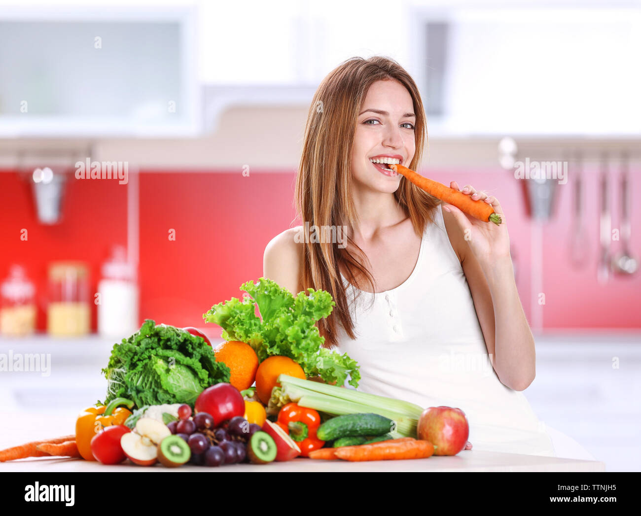 Woman eating carrot in the kitchen Stock Photo - Alamy