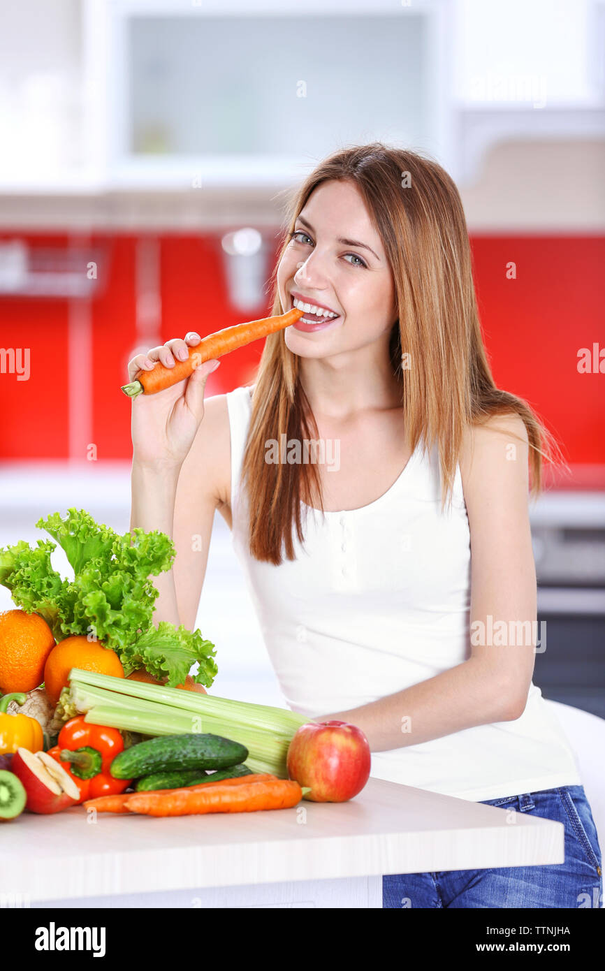 Woman eating carrot in the kitchen Stock Photo - Alamy