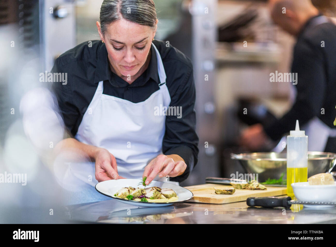 Female chef garnishing food while coworker working in background at ...