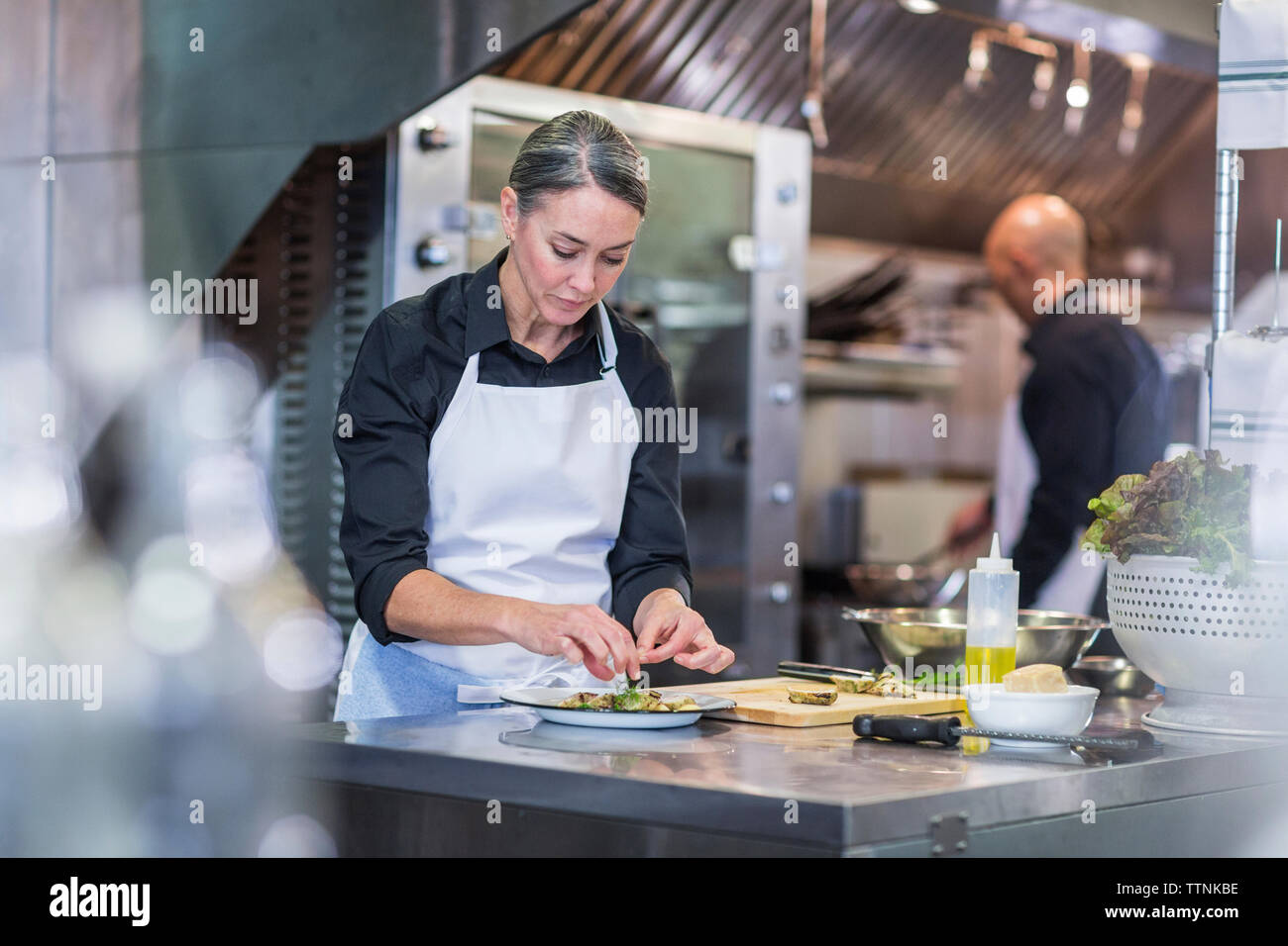 Female chef garnishing food while coworker working in background at ...