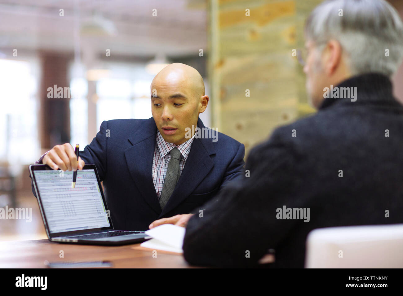 businessman explaining to male colleague over laptop computer in office ...