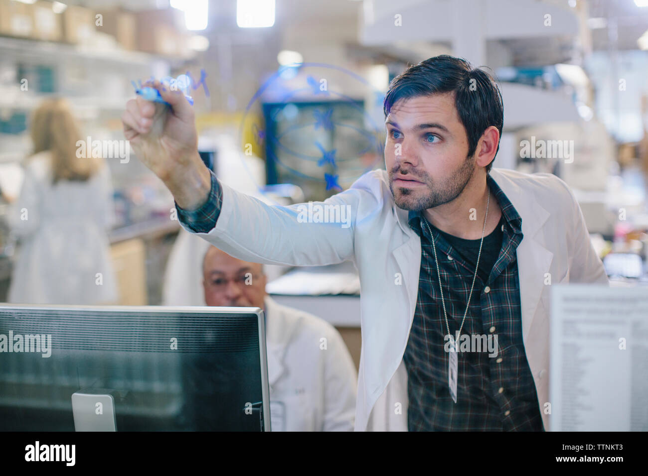 Male doctor writing on glass window with coworkers in background at ...
