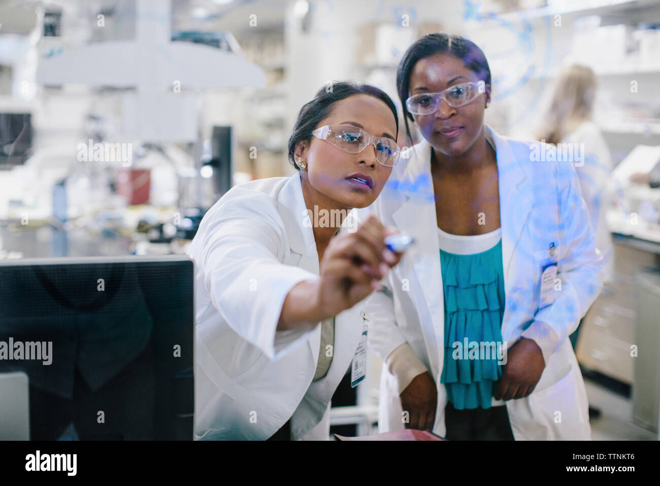 Female doctors discussing while writing on glass window in medical room ...