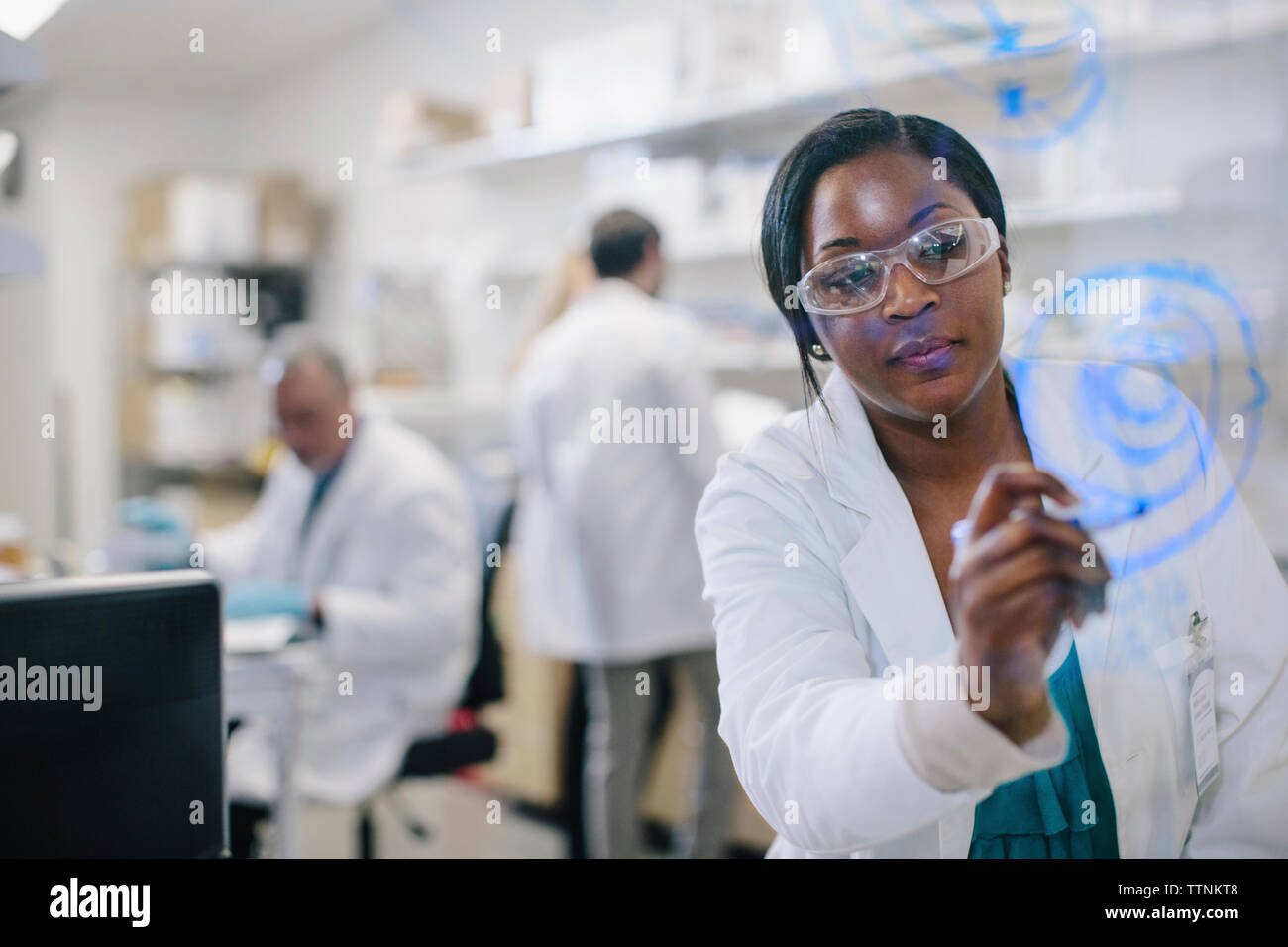 Female doctor writing on glass window with coworkers in background at ...