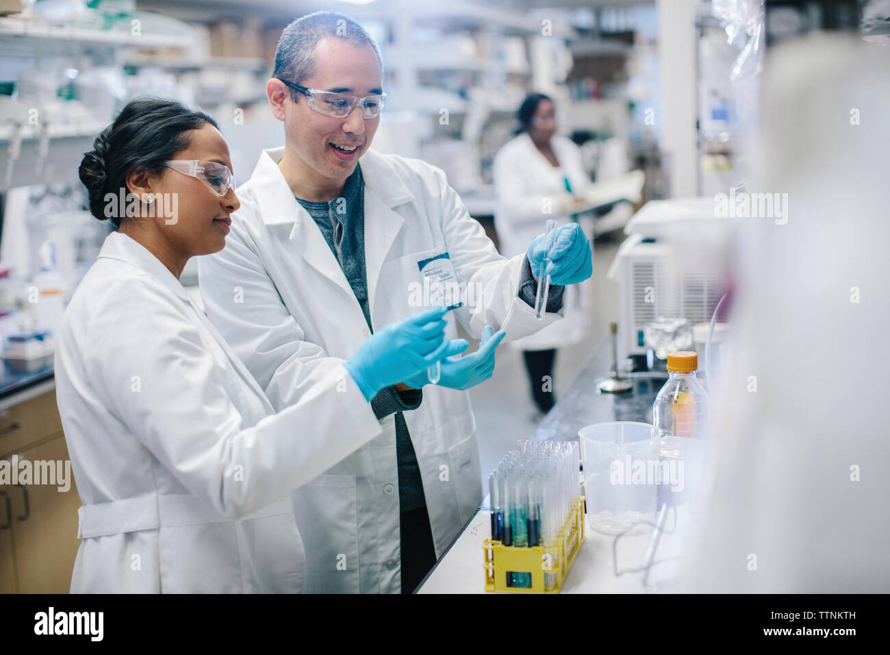 Doctors examining test tubes while coworker working in background at ...