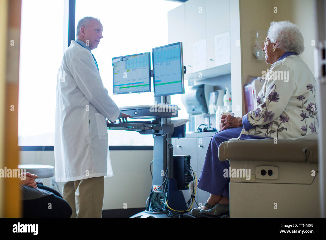 Male doctor talking to female patient while using computer in hospital ...