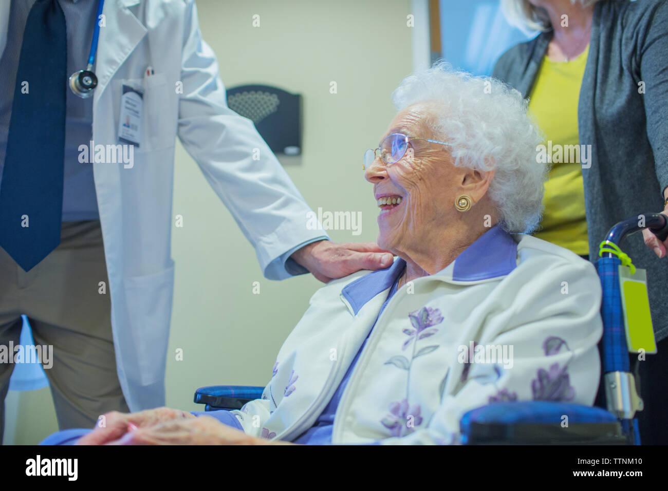 Male doctor standing by smiling female patient sitting on wheelchair in ...