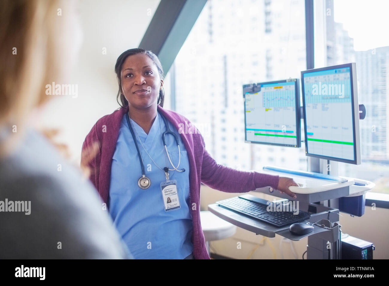 Female doctor looking at patient while standing by desktop computers in ...