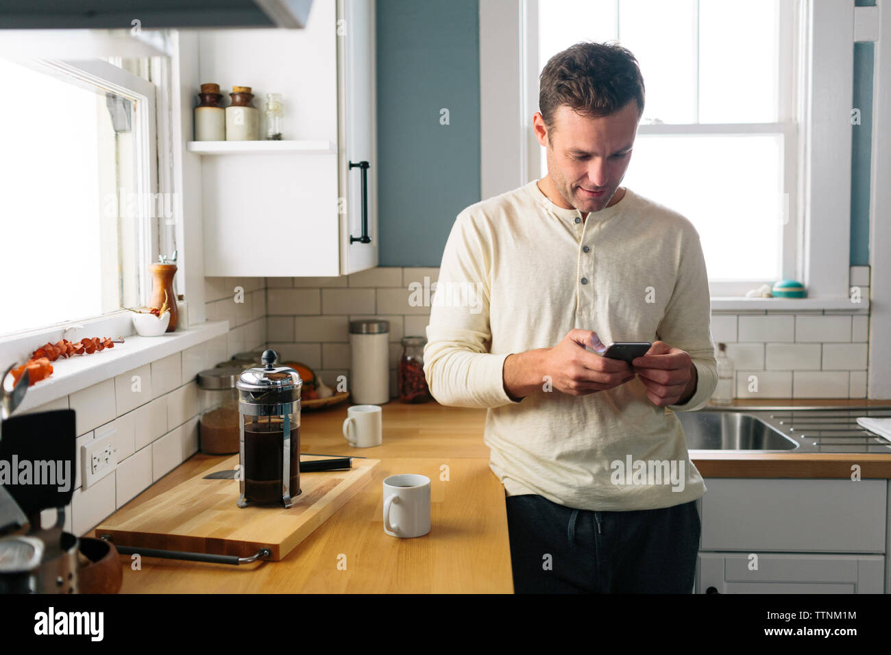 Man using smart phone while leaning by kitchen counter at home Stock ...