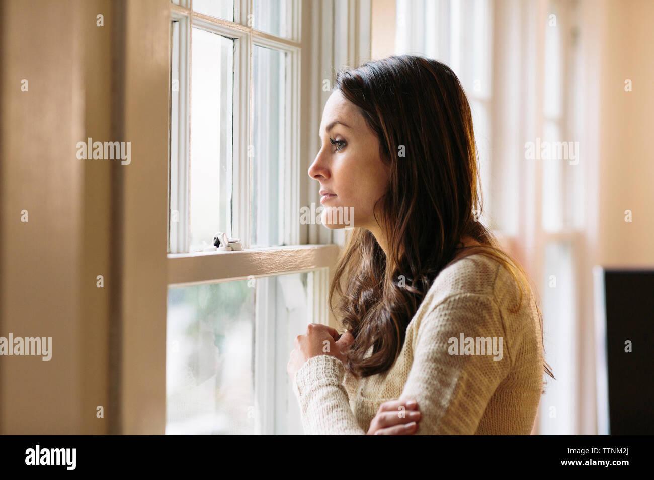 Side view of thoughtful woman standing by window at home Stock Photo ...