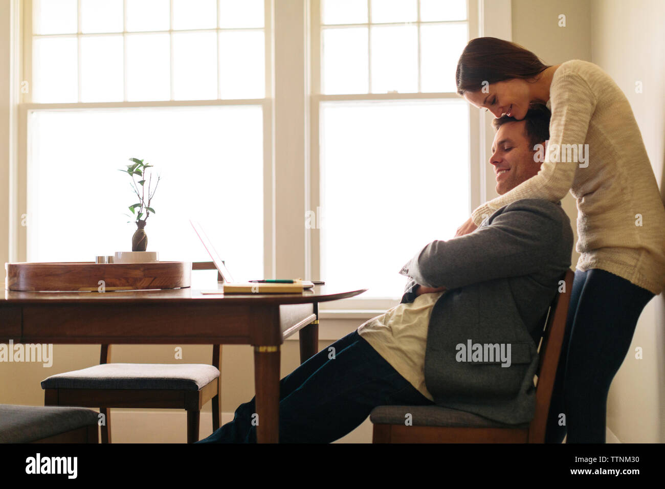 Side view of woman embracing man sitting on chair at home Stock Photo ...