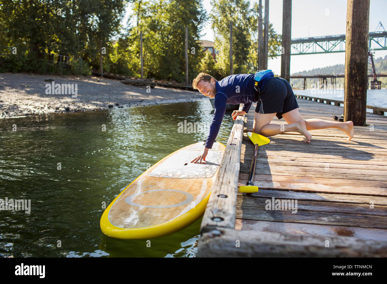 Side view of man touching paddleboard while leaning on pier Stock Photo ...