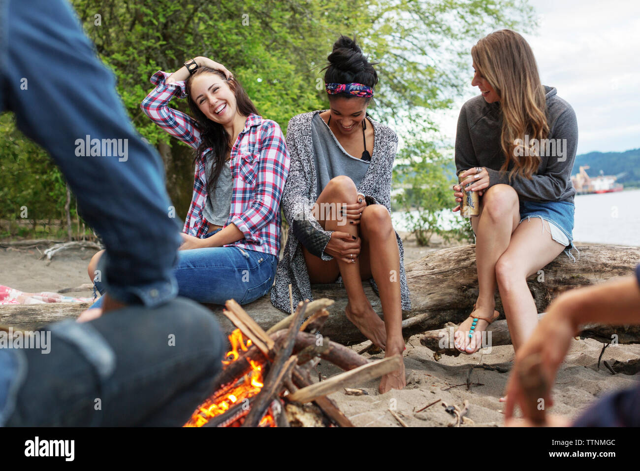 Happy friends sitting by campfire at riverbank Stock Photo - Alamy