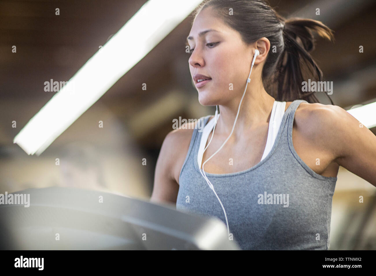 Confident woman listening music while exercising on treadmill in gym ...