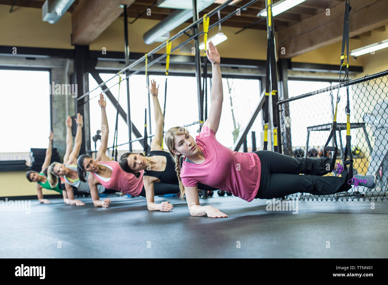 Women practicing side plank pose while balancing on resistance bands in ...