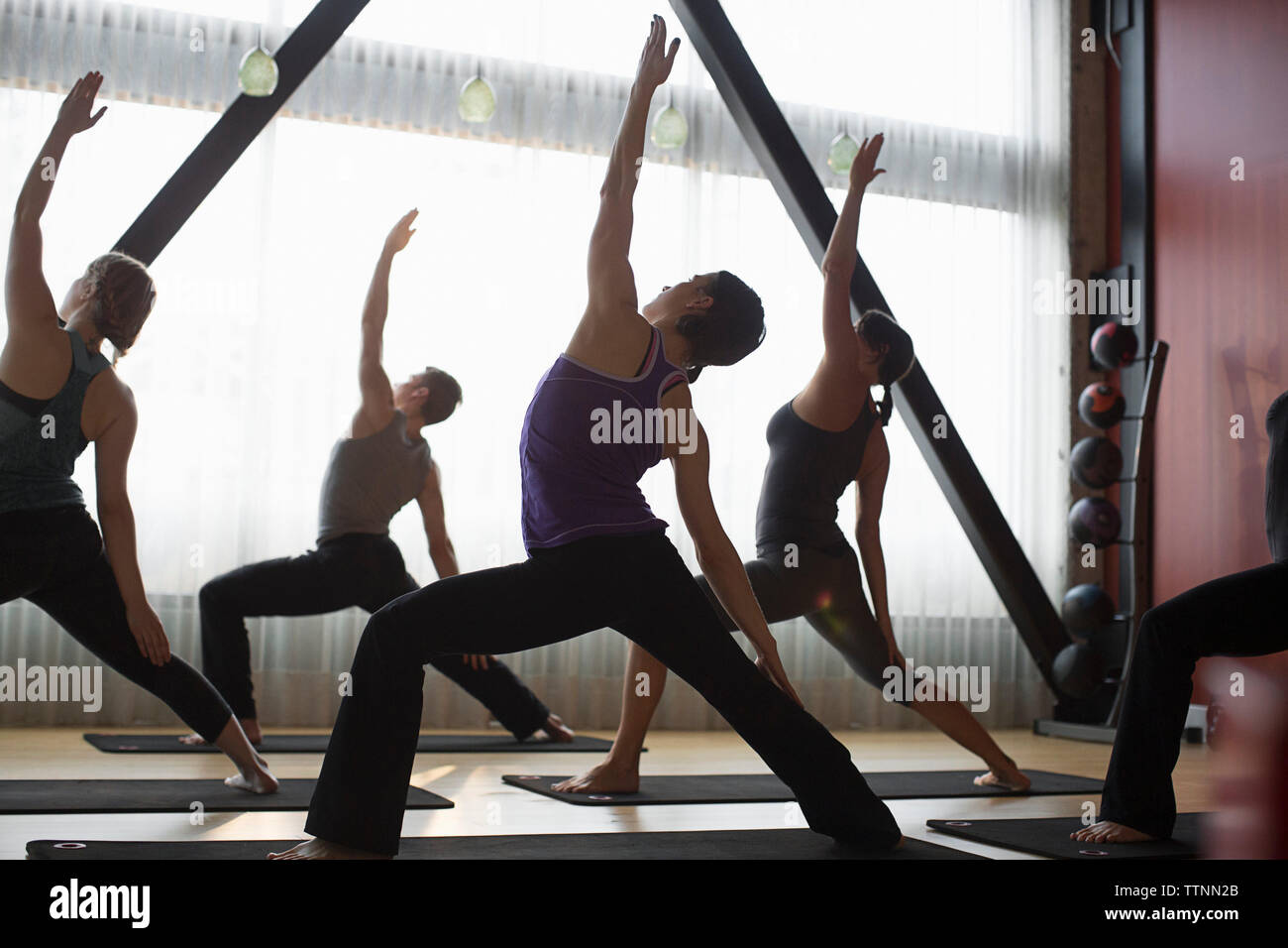 Rear view of male instructor with women practicing triangle position in ...