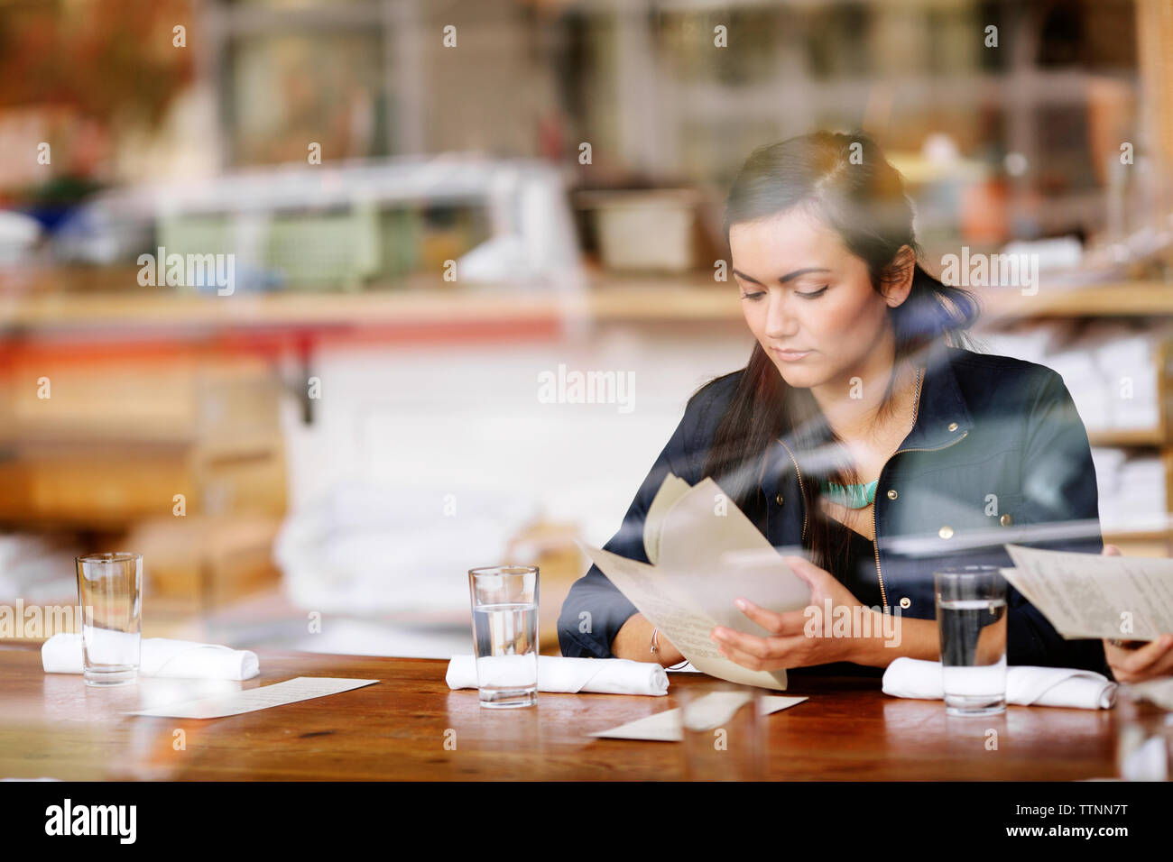 Woman looking at menu while sitting in restaurant seen through glass ...