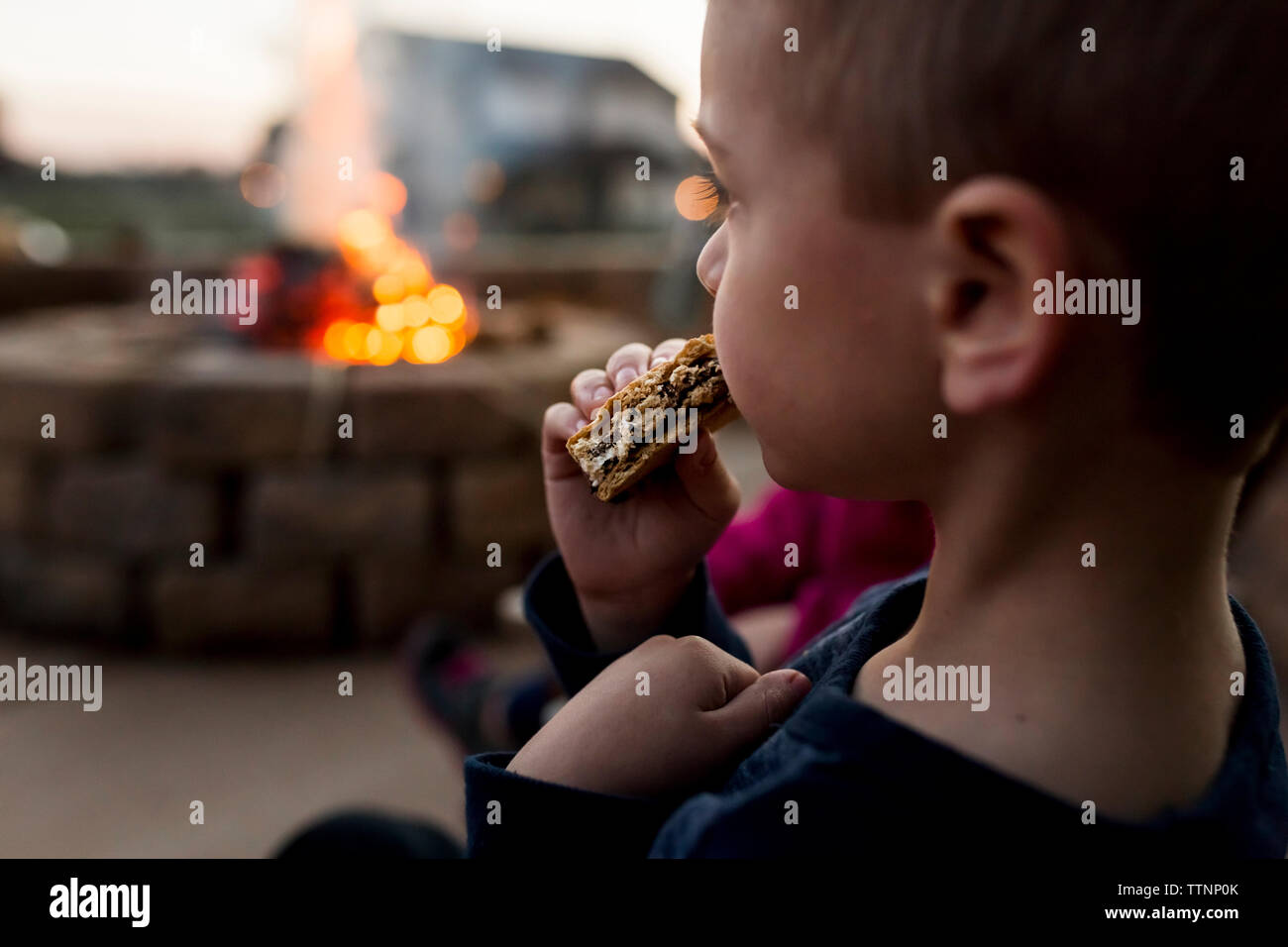 Boy eating smore at yard with fire pit in background Stock Photo - Alamy