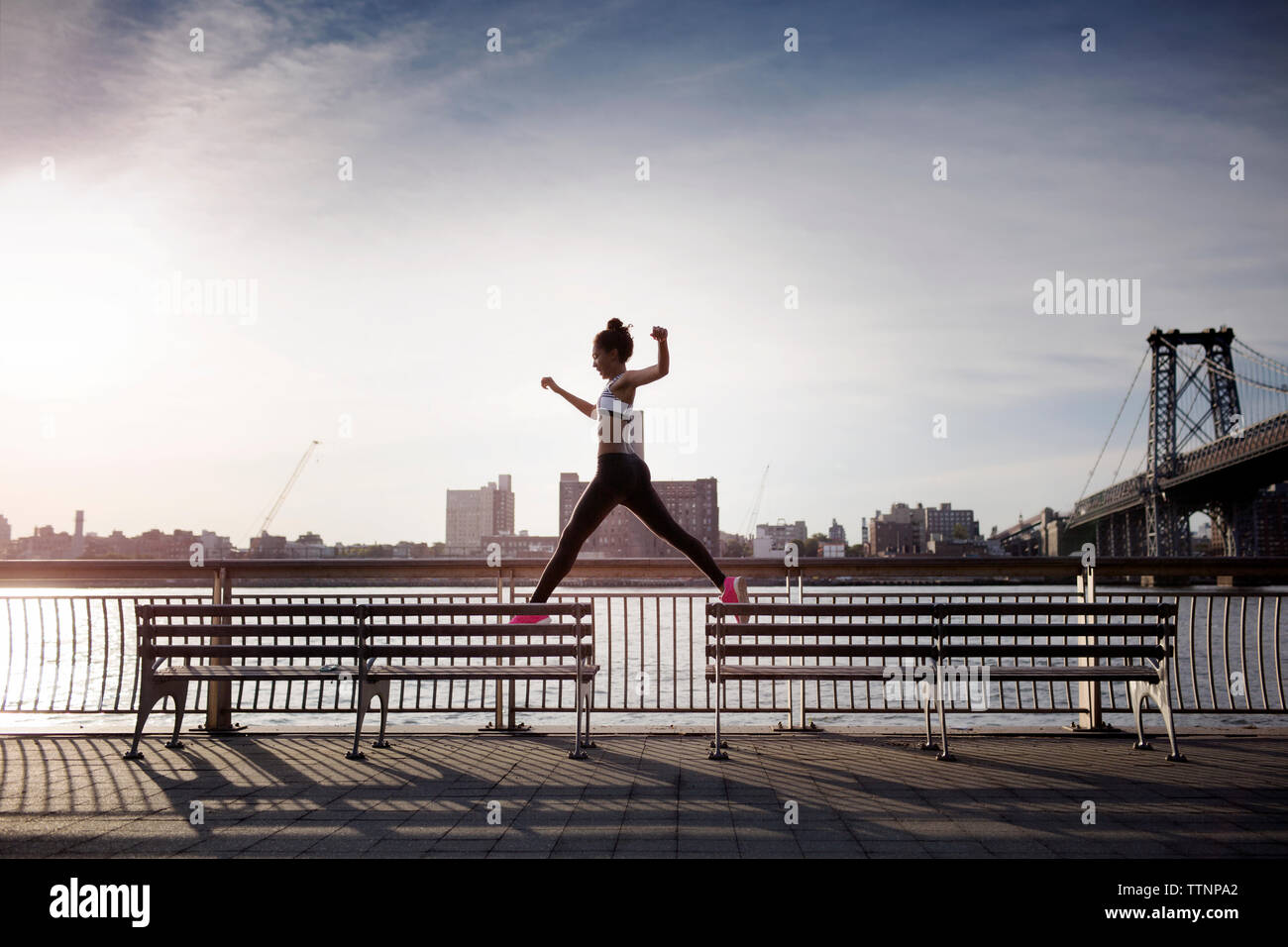 Sporty woman jumping on benches with Williamsburg Bridge in background ...