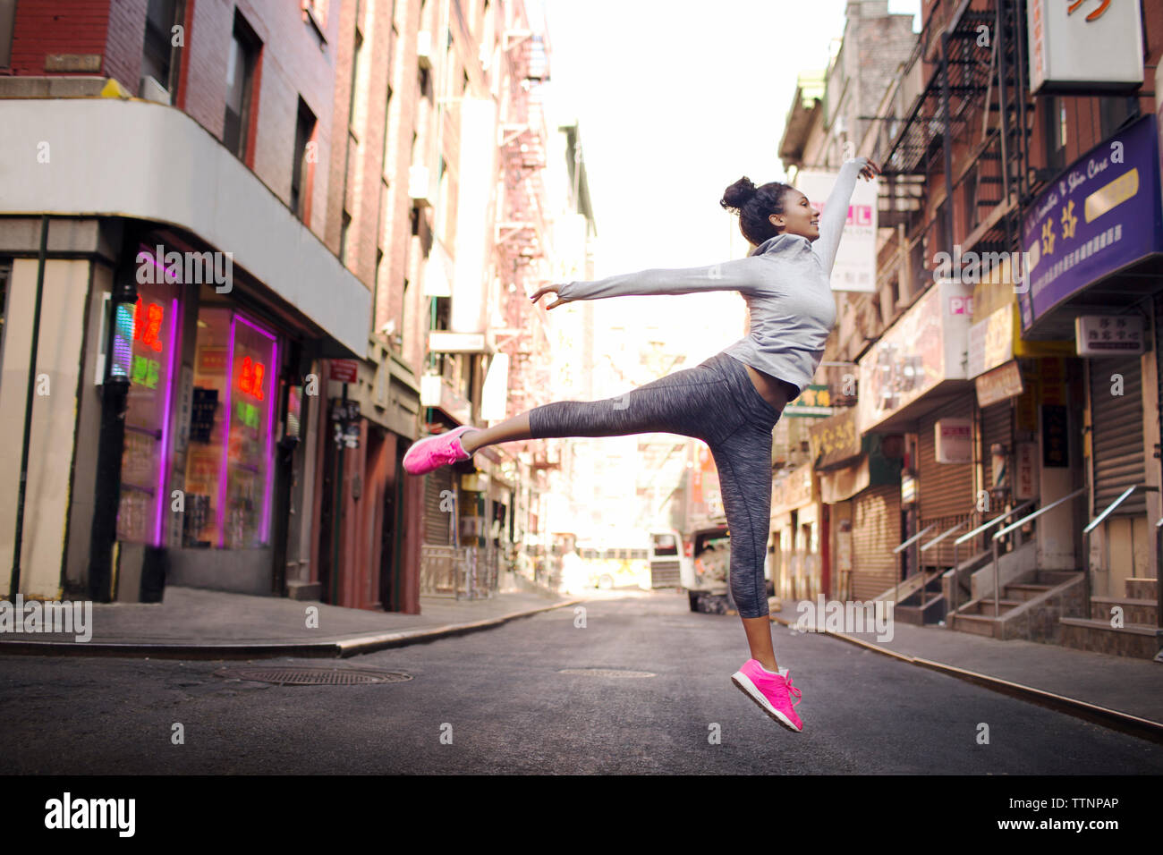 Female jogger jumping on street amidst buildings Stock Photo - Alamy