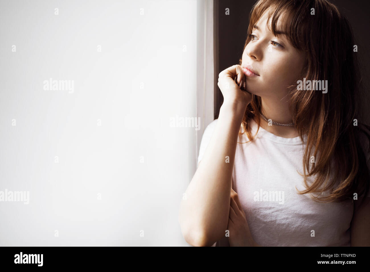 Thoughtful young woman looking out through window at home Stock Photo ...