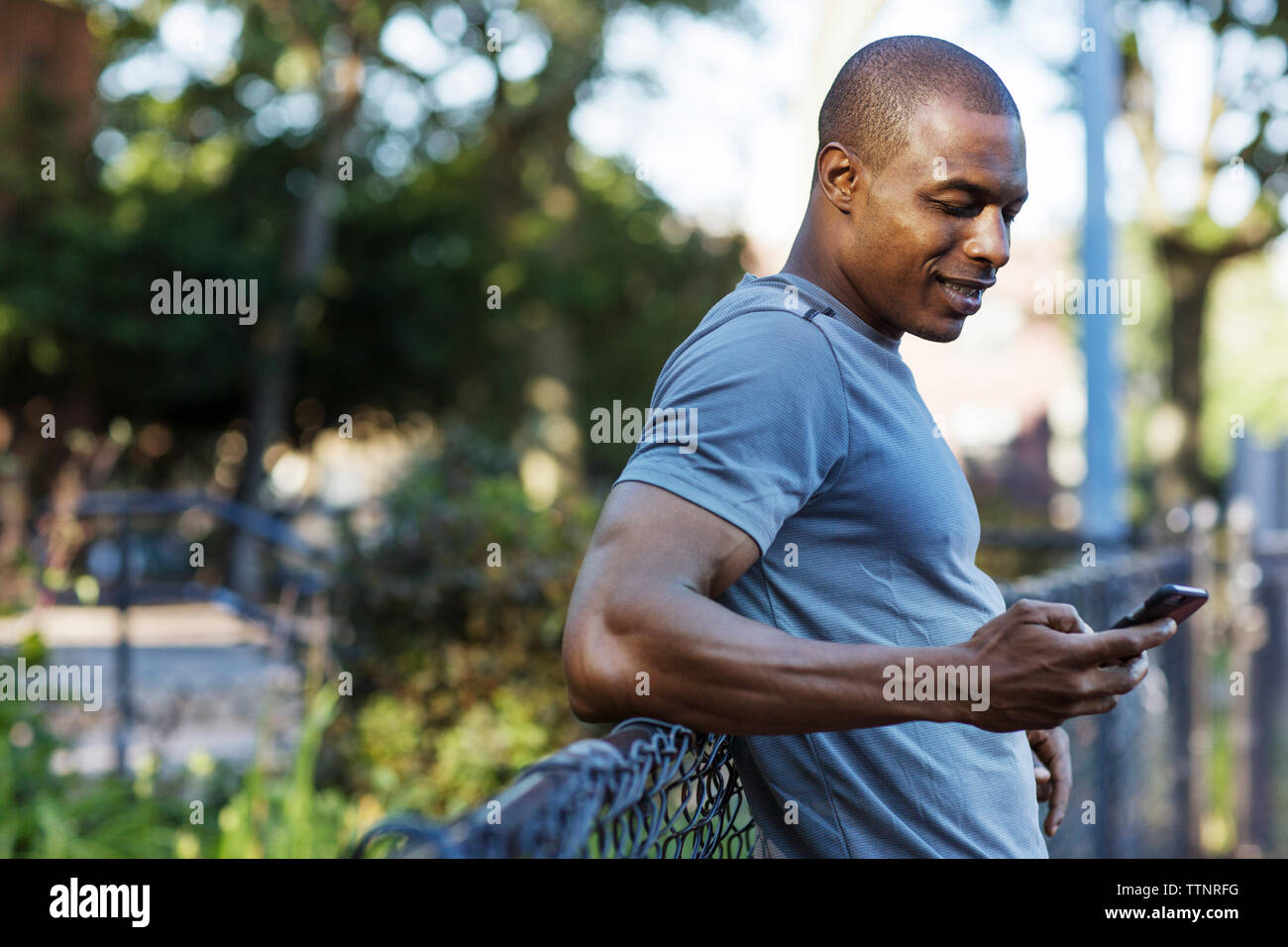 Side view of man using mobile phone while leaning on railing in park ...