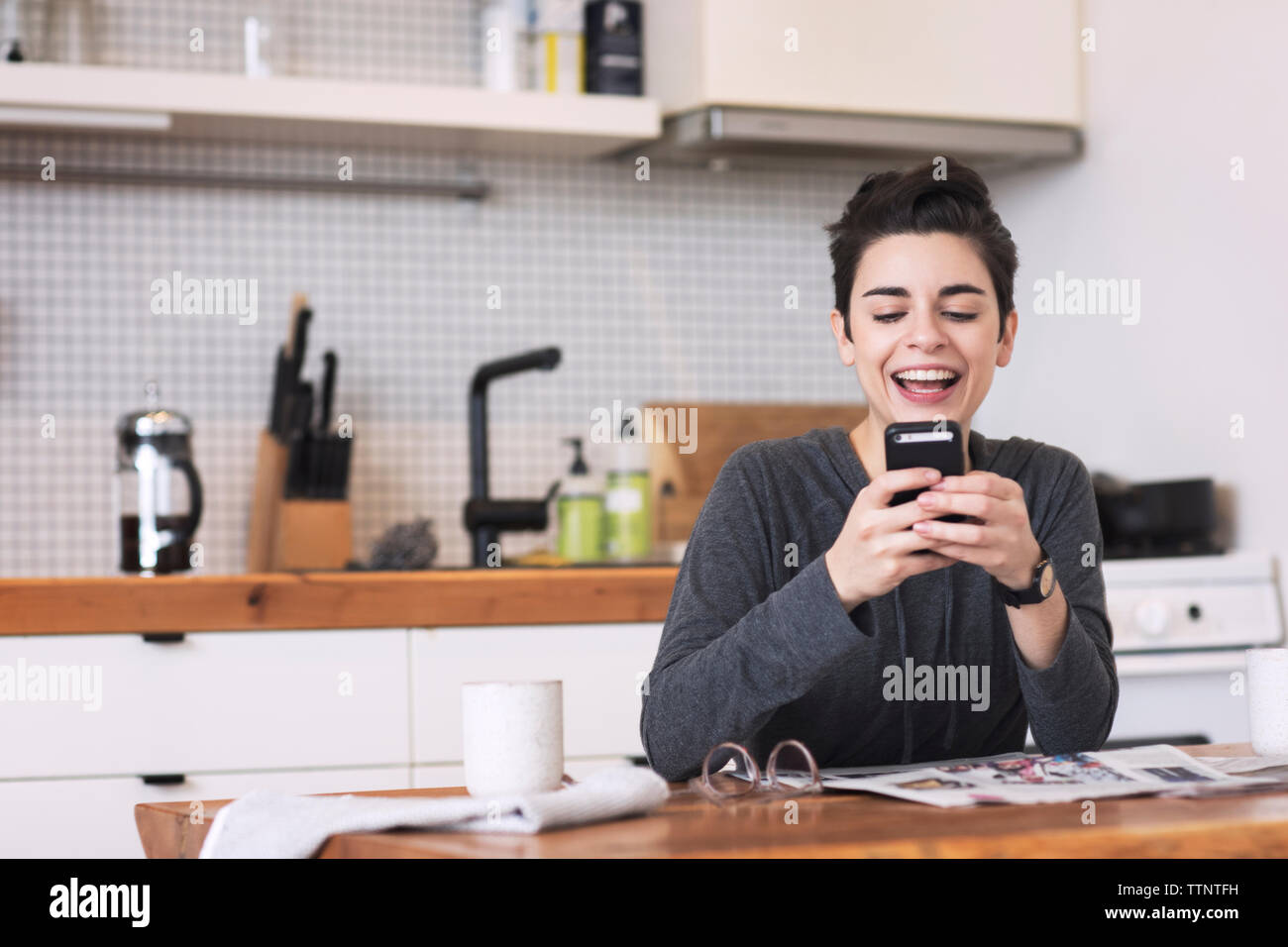 Happy woman using mobile phone at dining table in kitchen Stock Photo ...