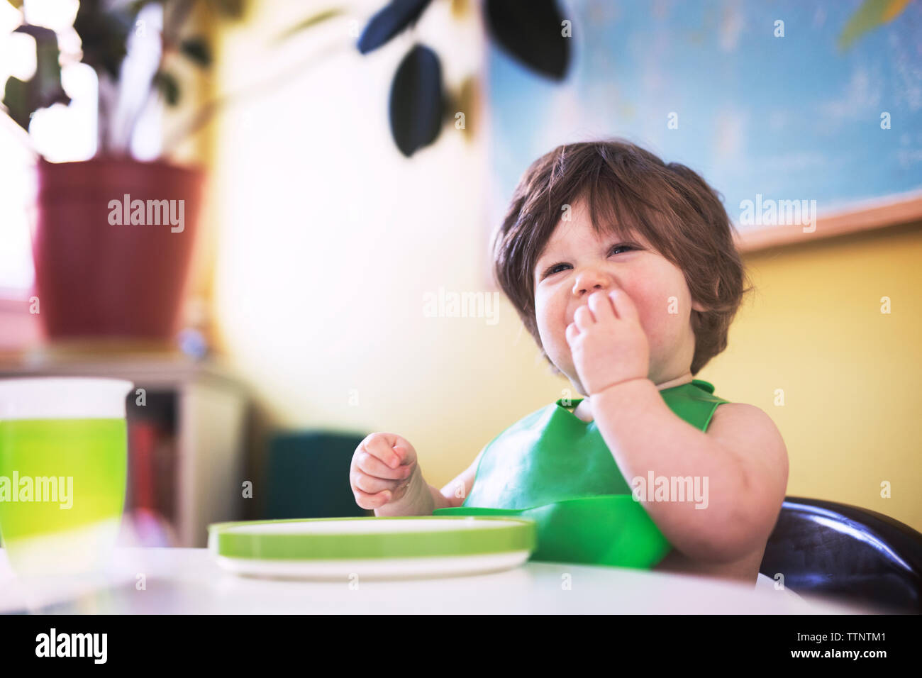 Baby boy eating food while sitting on high chair at home Stock Photo ...